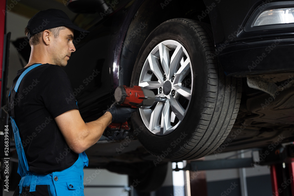 Car mechanic replacing car wheel of lifted automobile at repair service ...