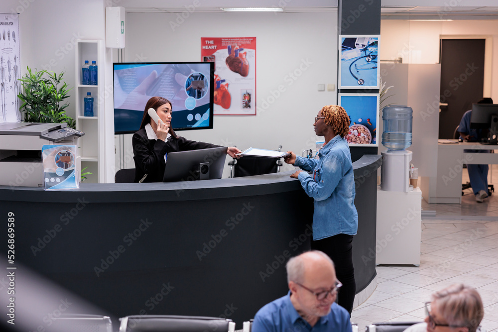 Receptionist using landline phone at reception desk, giving report ...