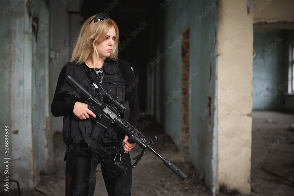 Young woman with the airsoft rifle is posing in the abandoned building ...