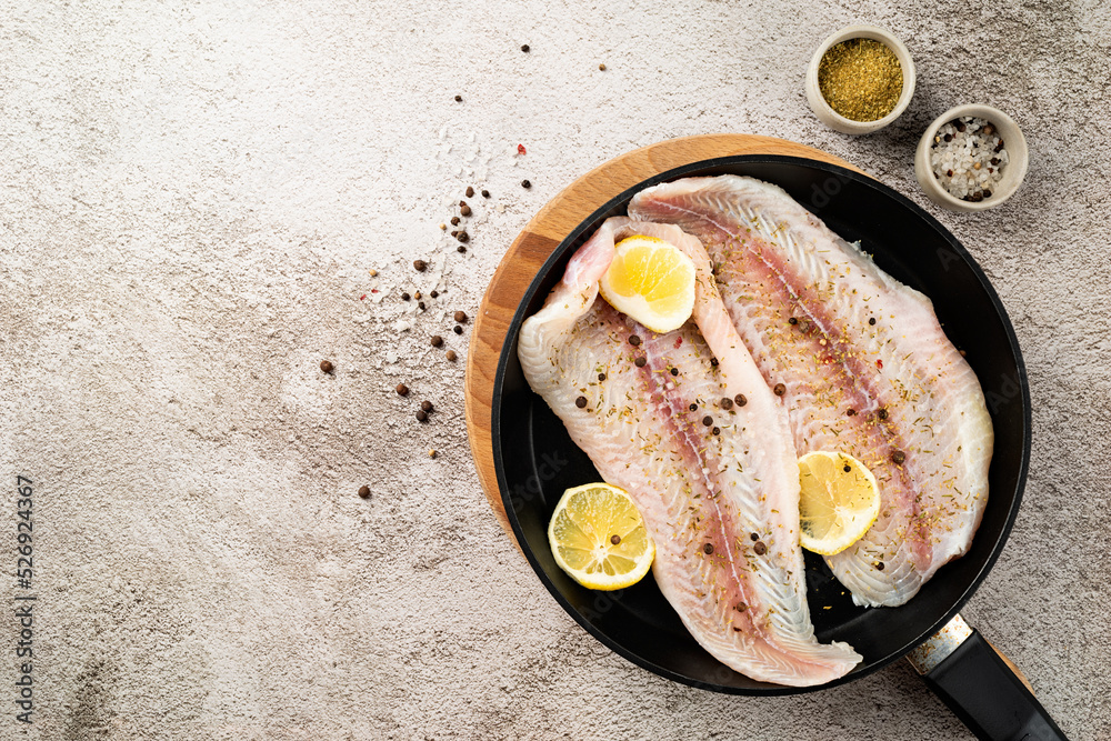 Foto de Raw pangasius fish fillet with lemon and spice in frying pan on ...