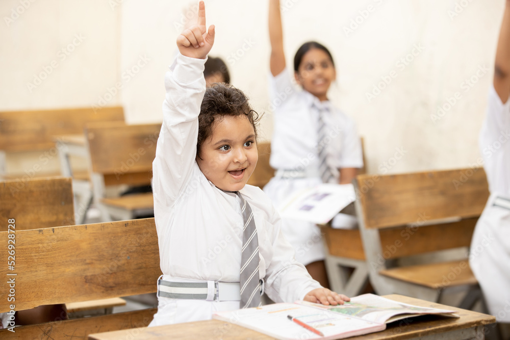 Happy indian schoolgirl raising arm to answer a question in the ...