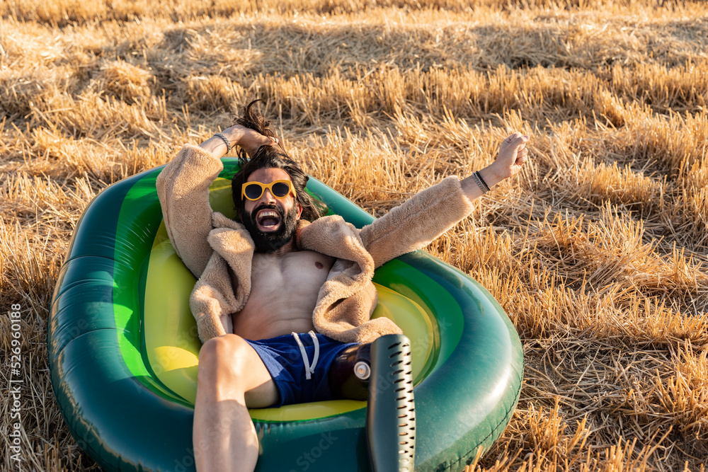 Happy bearded man with prosthetic leg lying on inflatable ring at field ...