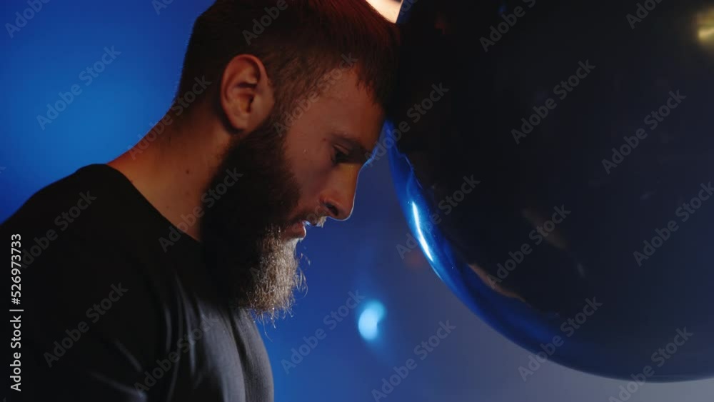 Side view of the tired male boxer rested her head on a punching bag ...