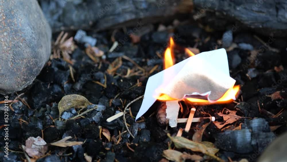 A white piece of paper burning on the charred surface of a fireplace in ...