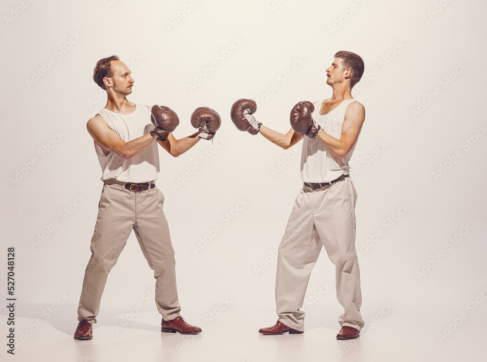 Portrait of two men playing, boxing in gloves isolated over grey studio ...