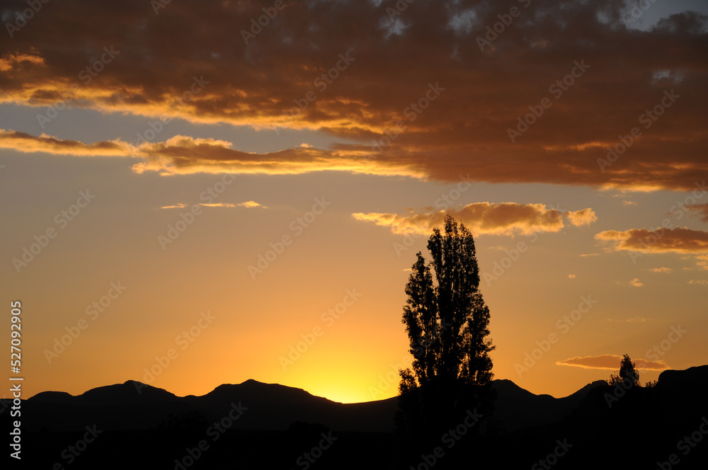Gentle sunset with silhouette of mountains and trees with clouds lined ...