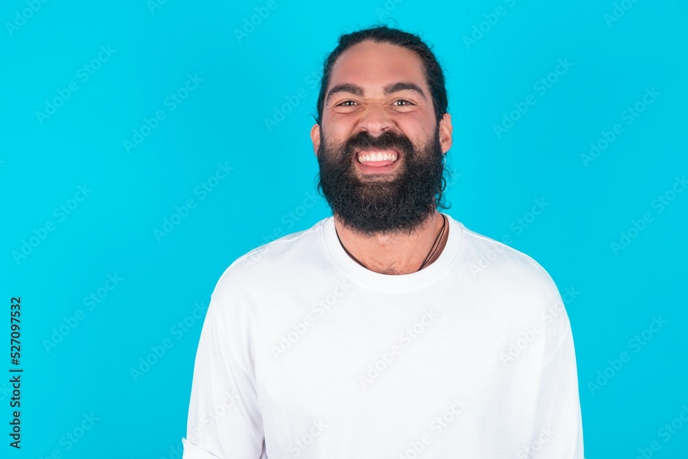 young bearded man wearing white T-shirt over blue studio background ...