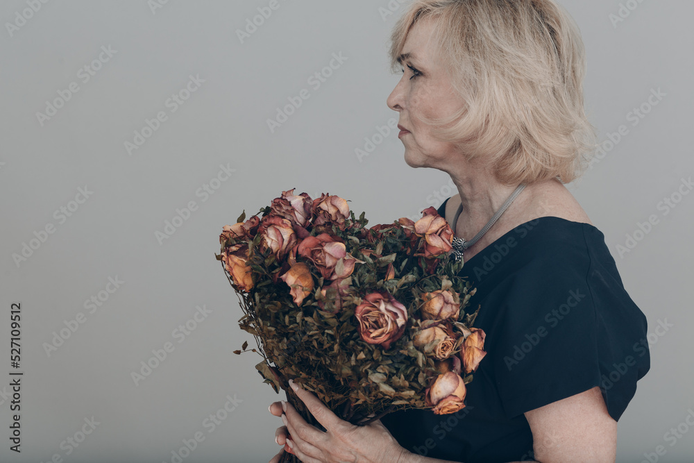 Sad elderly senior woman in white shirt holds withered one dry old dead ...