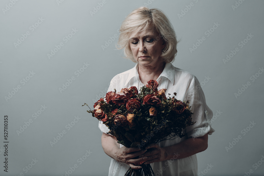 Sad elderly senior woman in white shirt holds withered one dry old dead ...