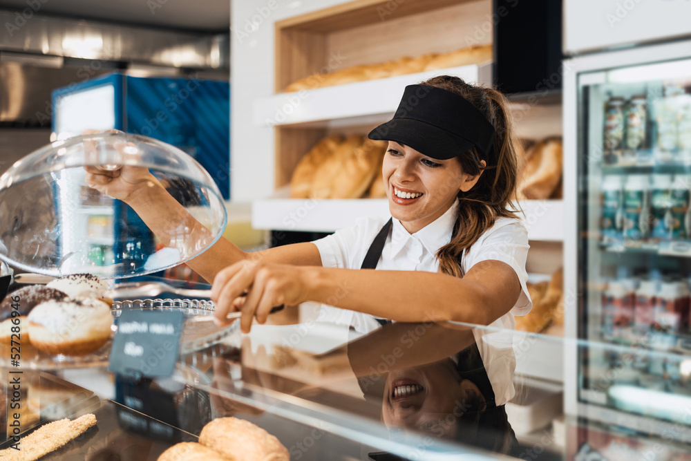 Beautiful young and happy female worker working in a modern bakery or ...
