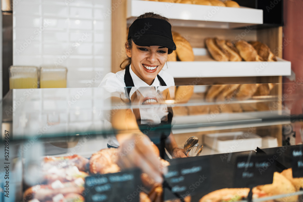 Beautiful young and happy female worker working in a modern bakery or ...