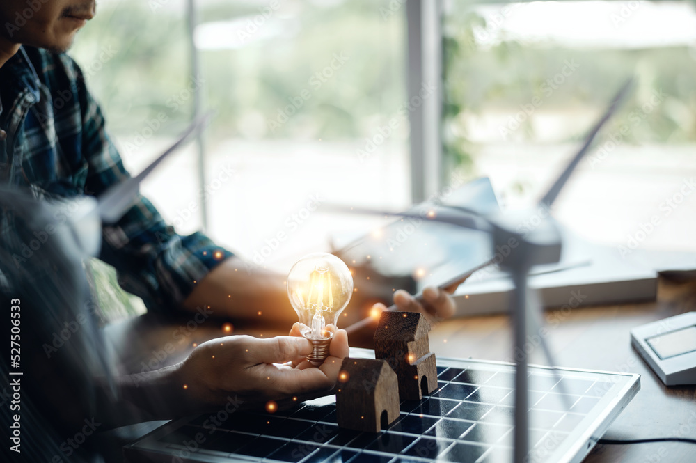 An engineer sits holding a light bulb and a tablet looking at a model ...