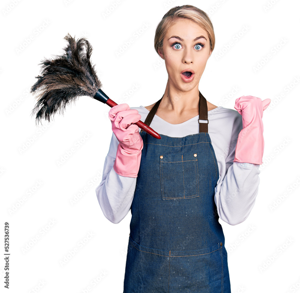 Beautiful young blonde woman wearing apron holding cleaning duster ...
