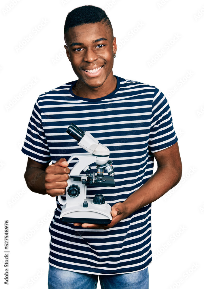 Young african american man holding microscope looking positive and ...