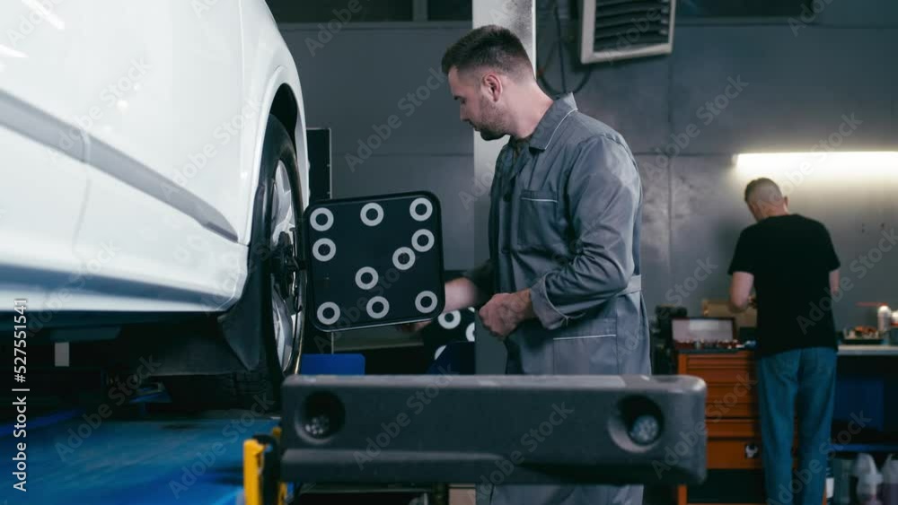A car service employee installs a wheel adapter with a target on the ...