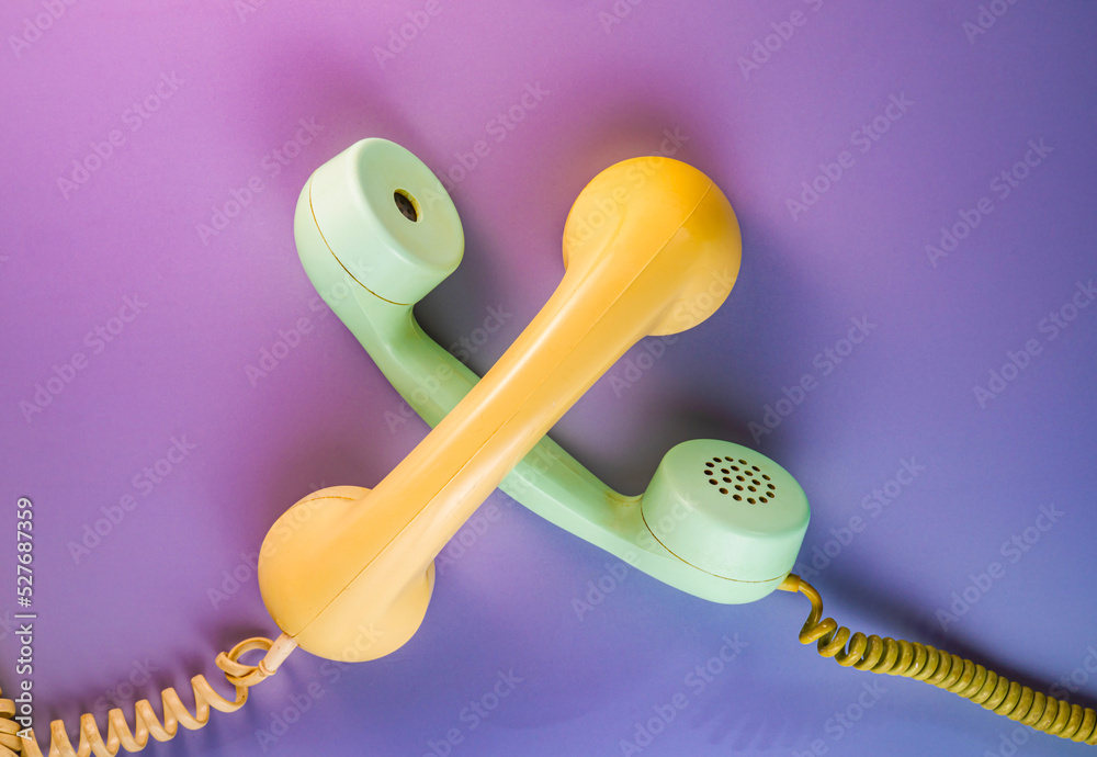 Yellow and green crossed telephone receivers with twisted cords from an ...