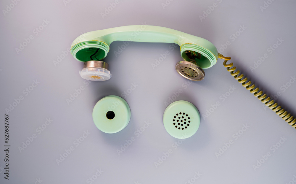 An old broken green telephone receiver with twisted cord on a gray ...