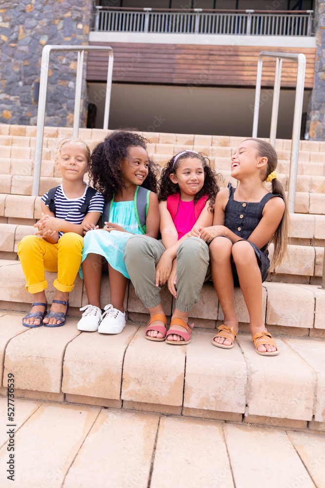 Full length of multiracial smiling elementary schoolgirls sitting on ...
