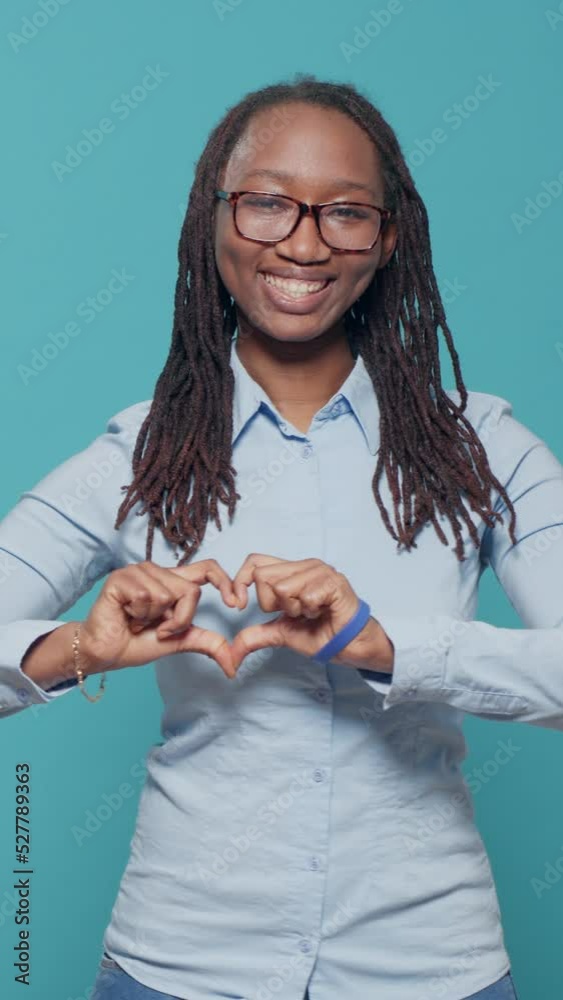 Vertical video: Woman doing heart shape with hands on camera, showing ...