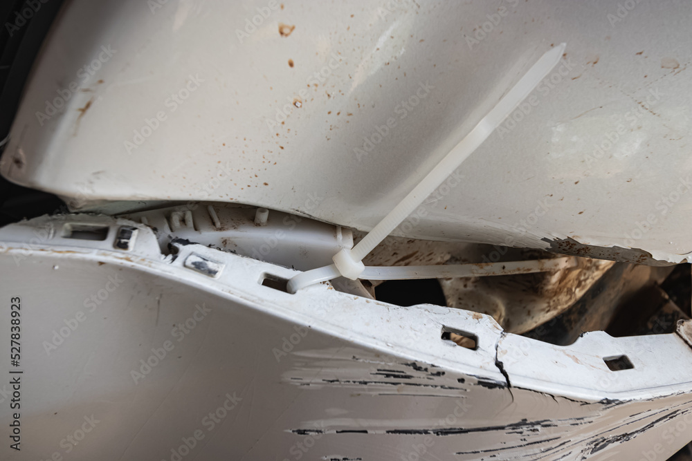 Using cable ties to fasten the front bumper parts of a car that has an ...