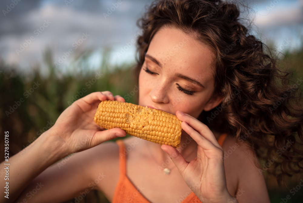 Girl with corn in a cornfield. The girl eats corn on the background of ...