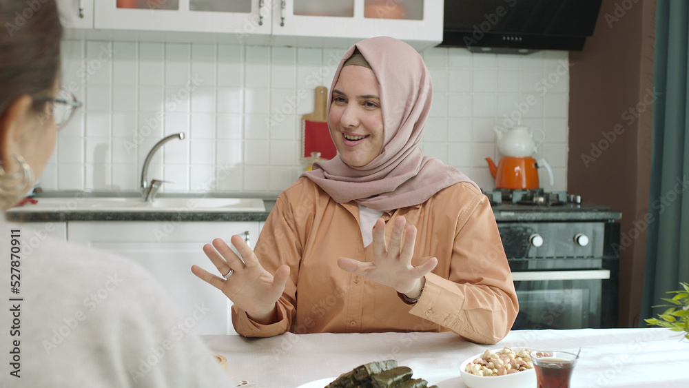 Over-the-shoulder view of a Muslim hijab-dressed woman chatting with ...