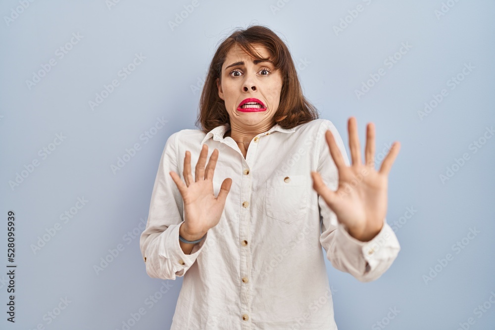 Young beautiful woman standing casual over blue background afraid and ...