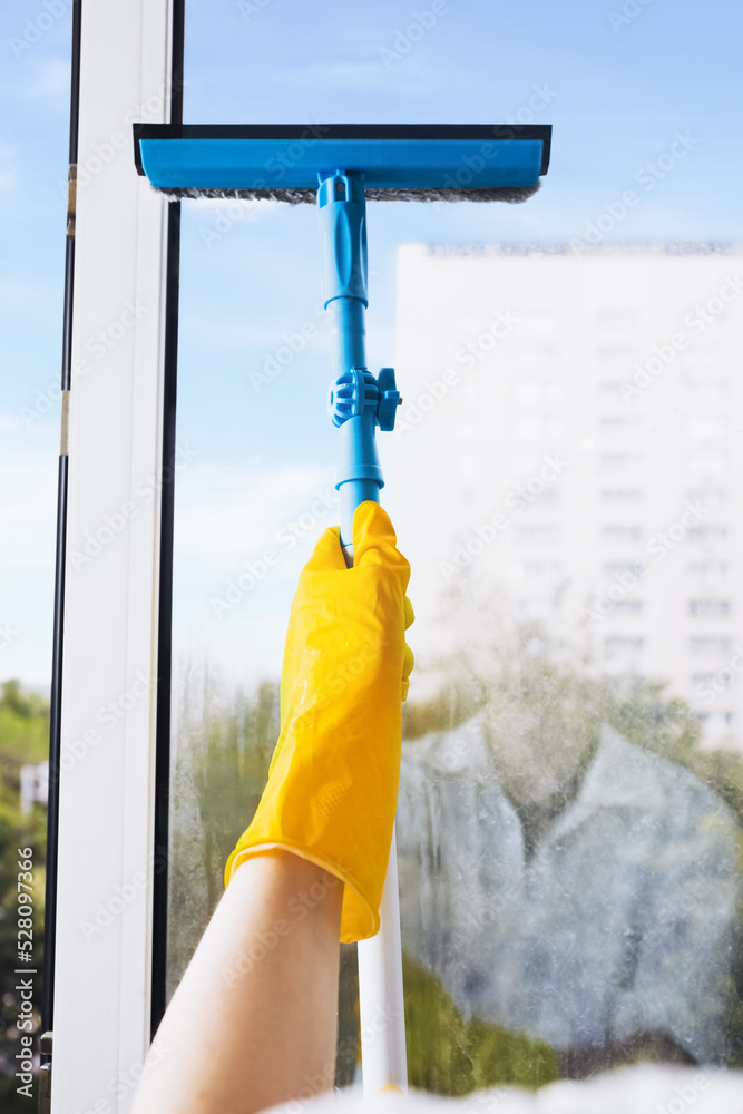 Man in yellow gloves cleaning window with squeegee and spray detergent ...