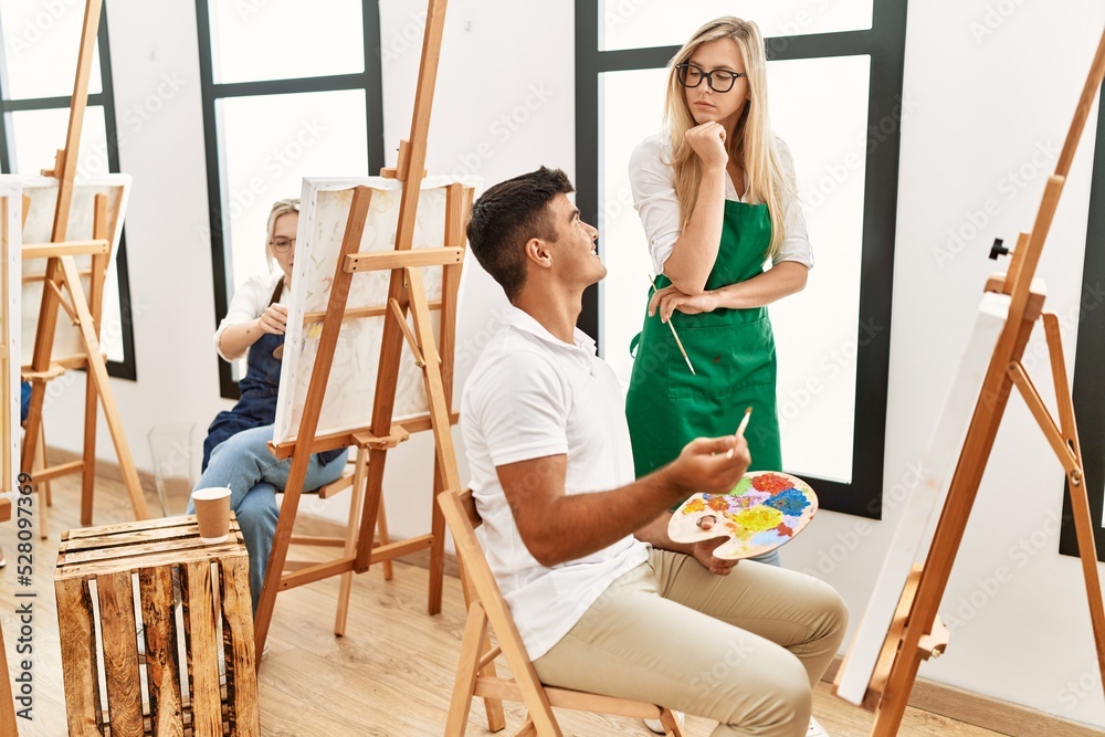 Art woman teacher with serious expression looking draw of paint student ...