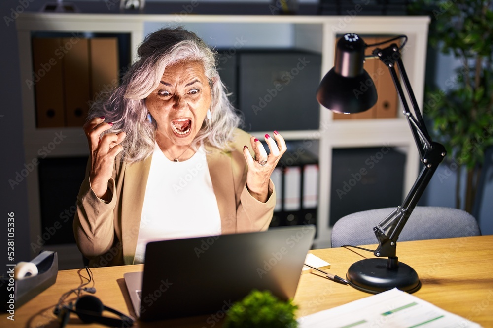 Middle age woman with grey hair working using computer laptop late at ...