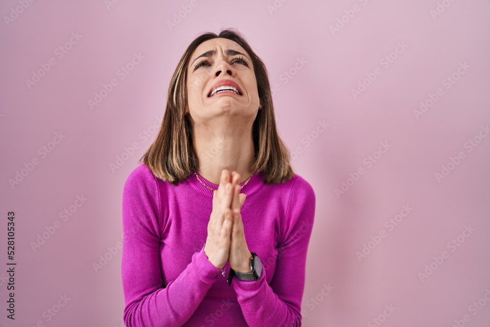 Hispanic woman standing over pink background begging and praying with ...