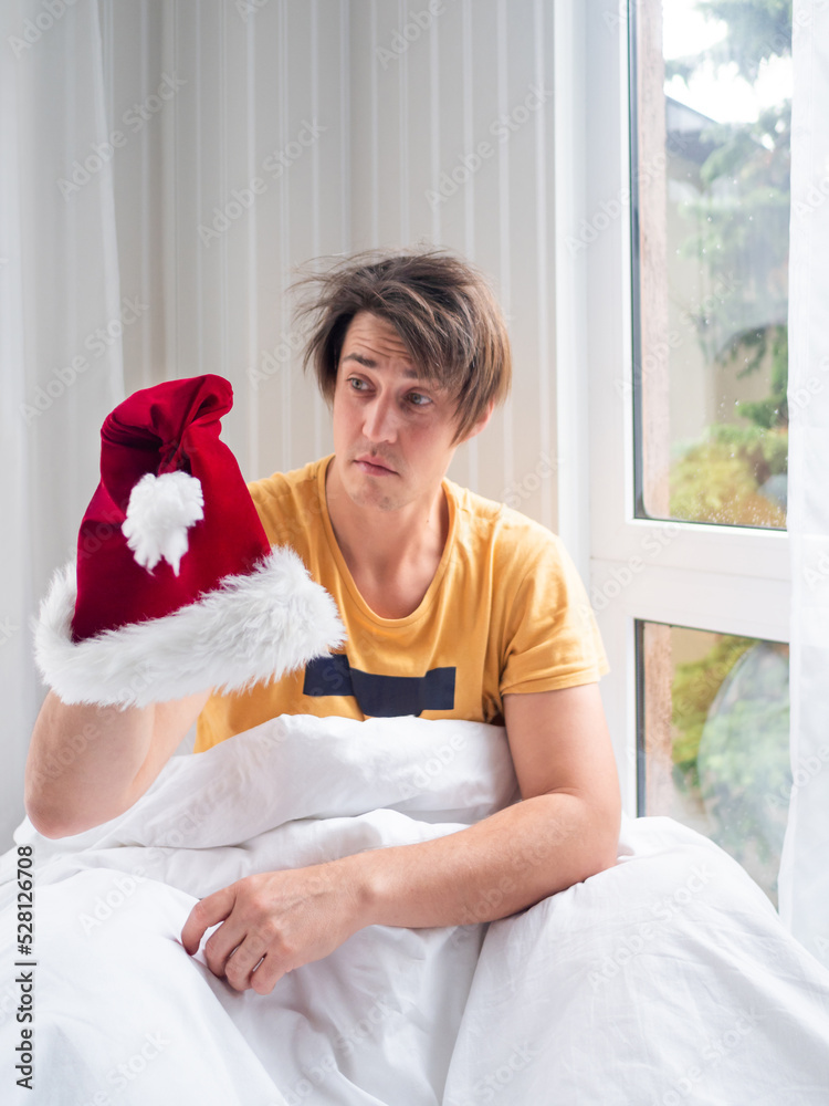 Man in Santa hat is waking up after Christmas party. He is suffering of ...