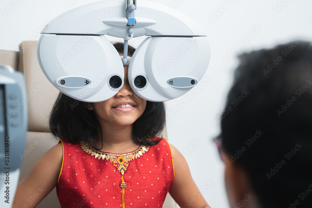 Happy Indian child girl doing subjective refraction with phoropter ...