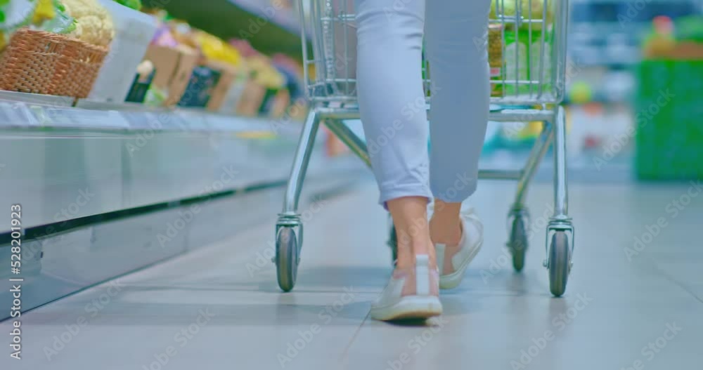 Women's feet in sneakers walking around the supermarket. Woman drives a ...