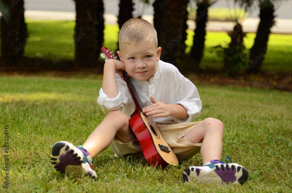 Little boy plays the acoustic guitar in the park. The child learns to ...