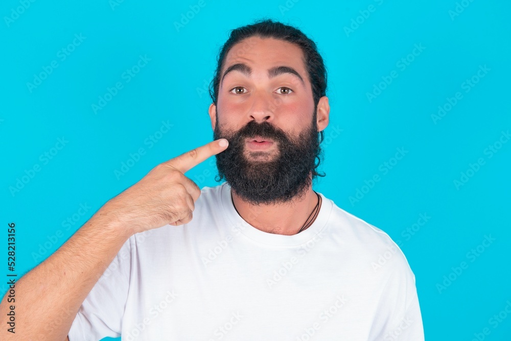 Charming young bearded man wearing white T-shirt over blue studio ...