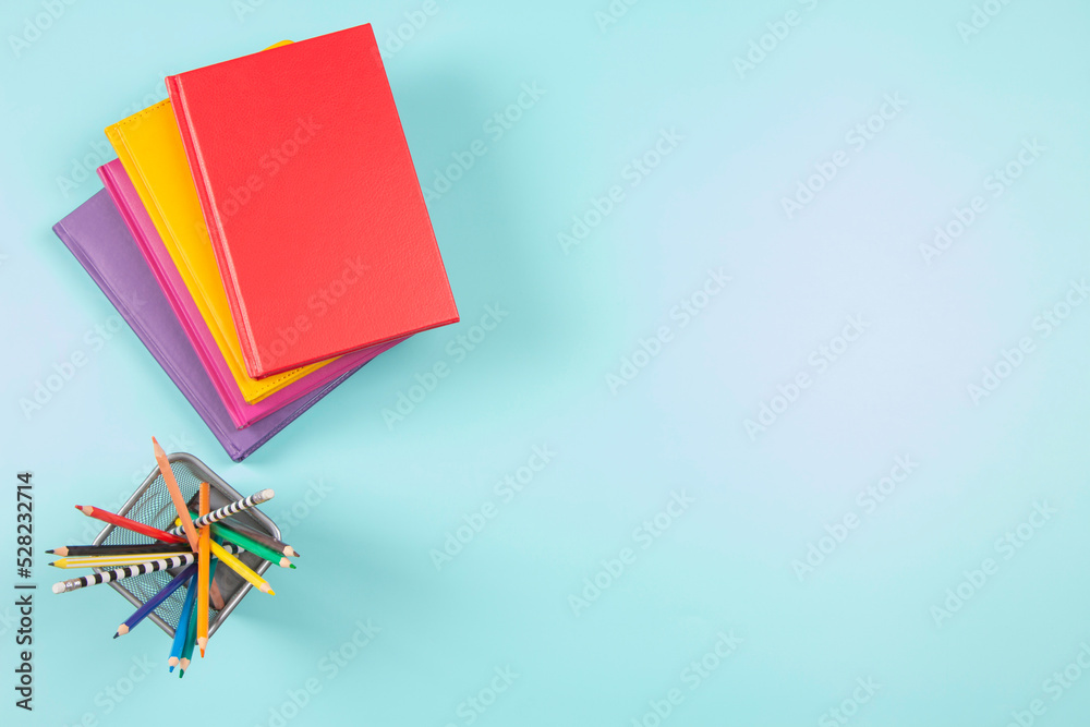 Colorful books and colored pencils in wire mesh cup on light blue ...