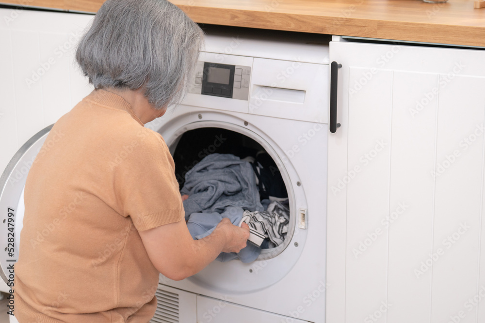 Contented senior housewife doing laundry in the laundry room with ...
