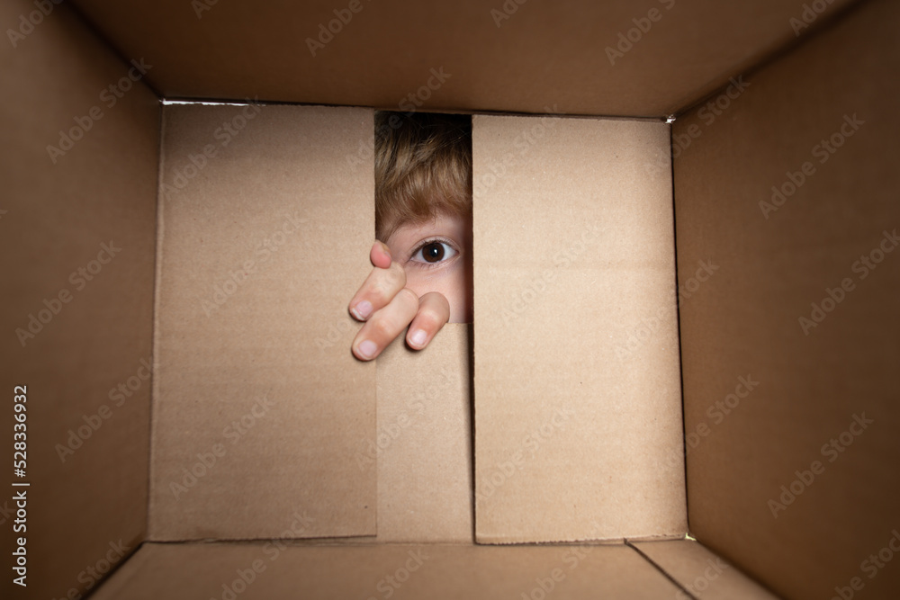 Amazed adorable little boy peeking inside gift box, unpacking present with funny astonished ...