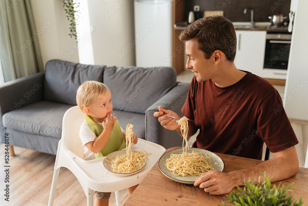 Upper view of handsome dad and cute blond baby in high chair eating ...