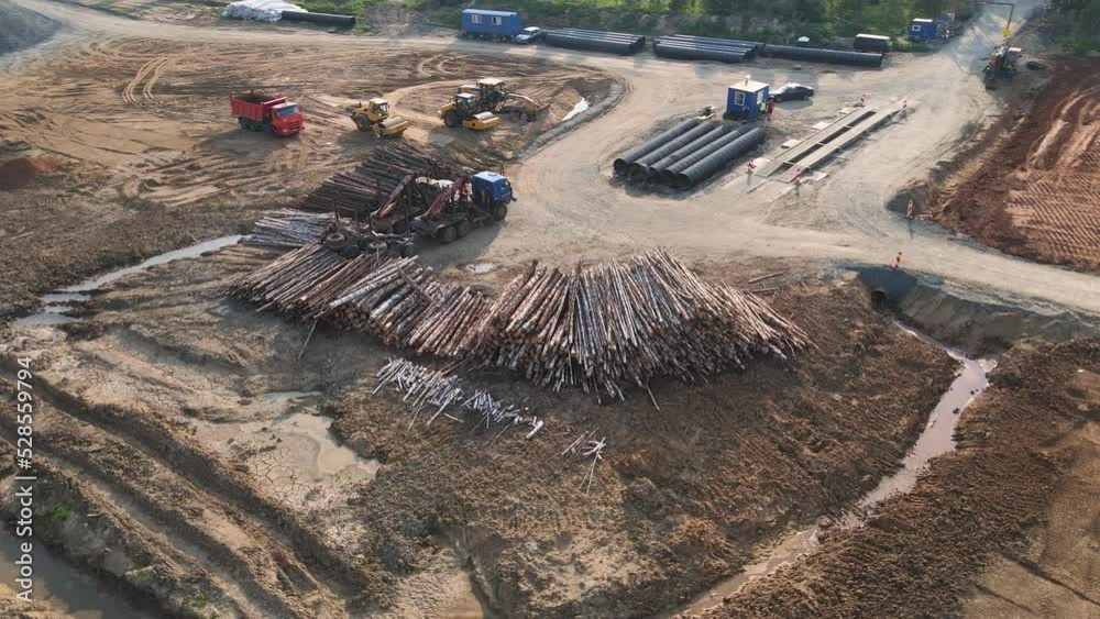 Construction site with a large stack of felled trees and industrial ...