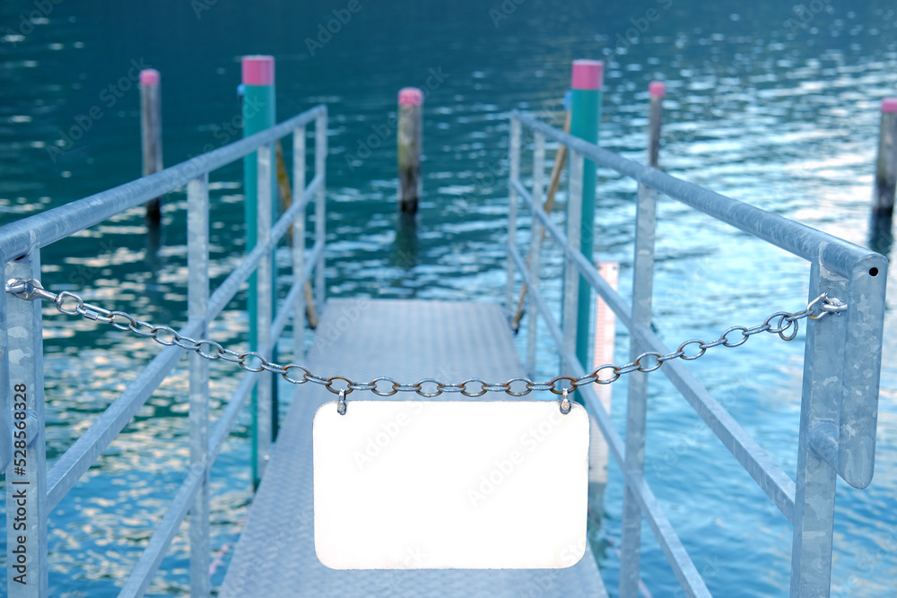 metal pier with a railing is closed with a chain. A white empty sign ...