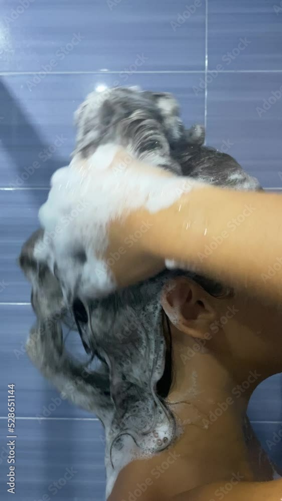 Woman in the shower rubbing her hair and lathering it with foamy ...