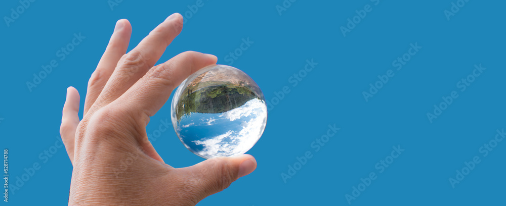 a hand is holding a glass sphere in which a landscape and blue sky with ...