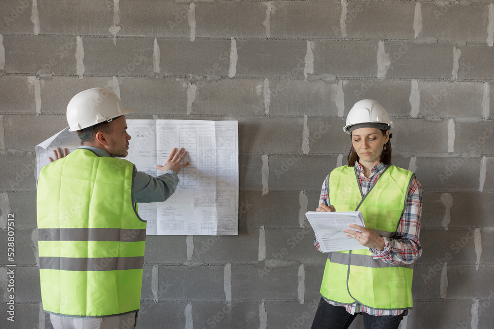 two engineers, a man and a woman in white helmets and protective vests ...