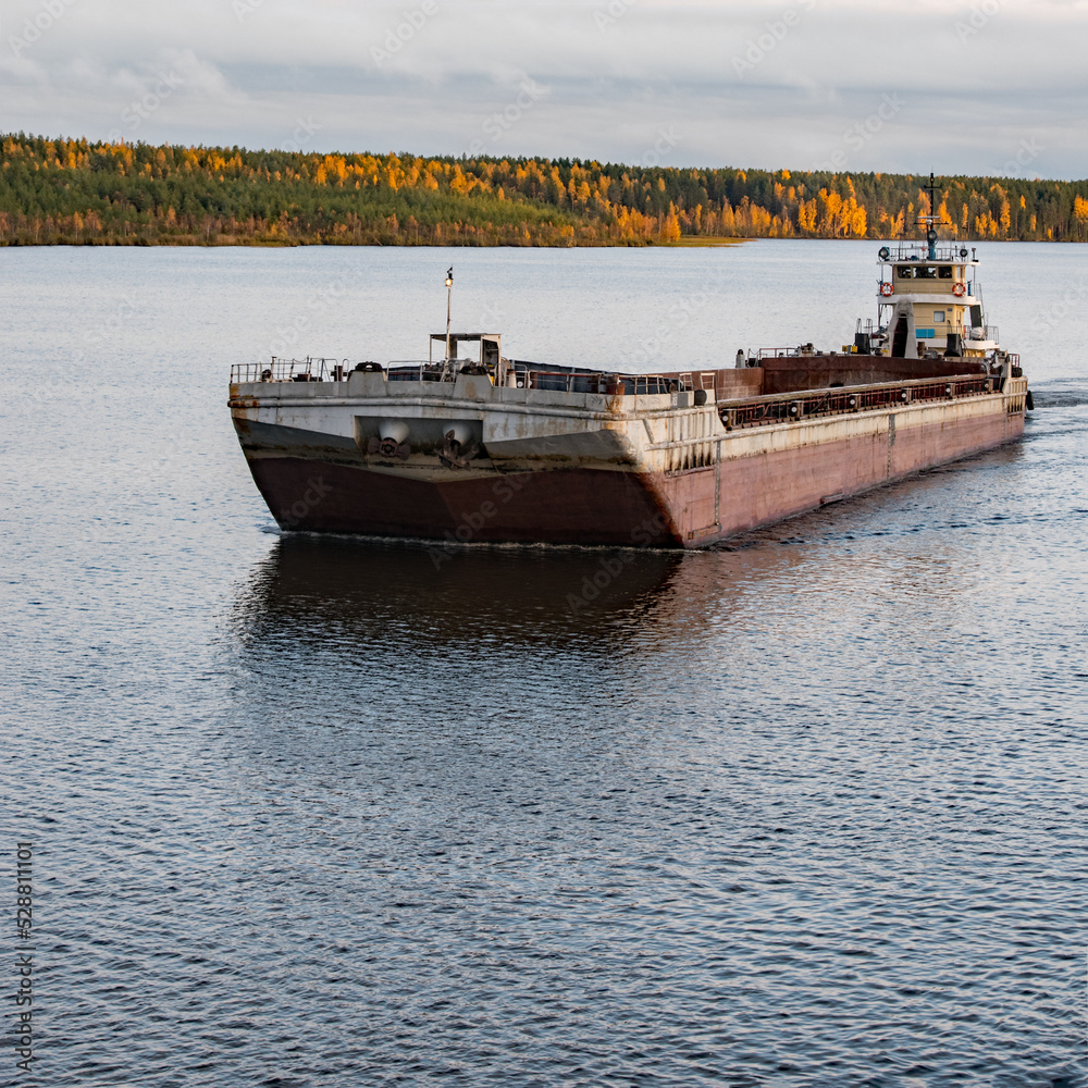 A freighter moves along a river in Europe with the colors of autumn in ...