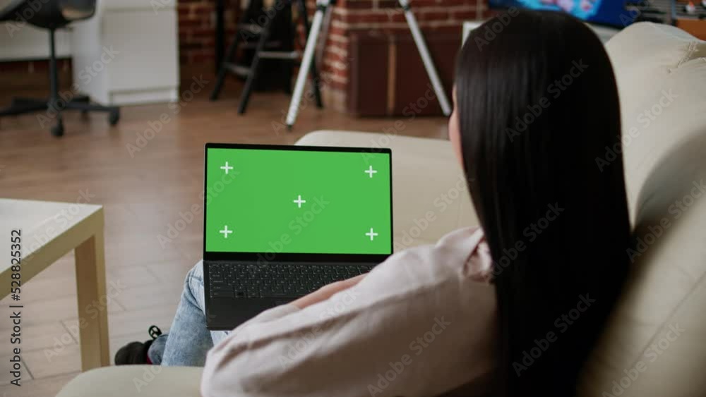 Woman sitting on sofa at home while looking at laptop having green ...