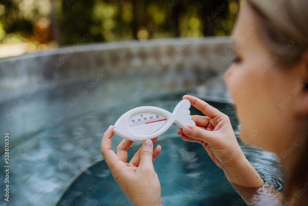 Young woman in bathtub, checking temperature of water with thermometer ...