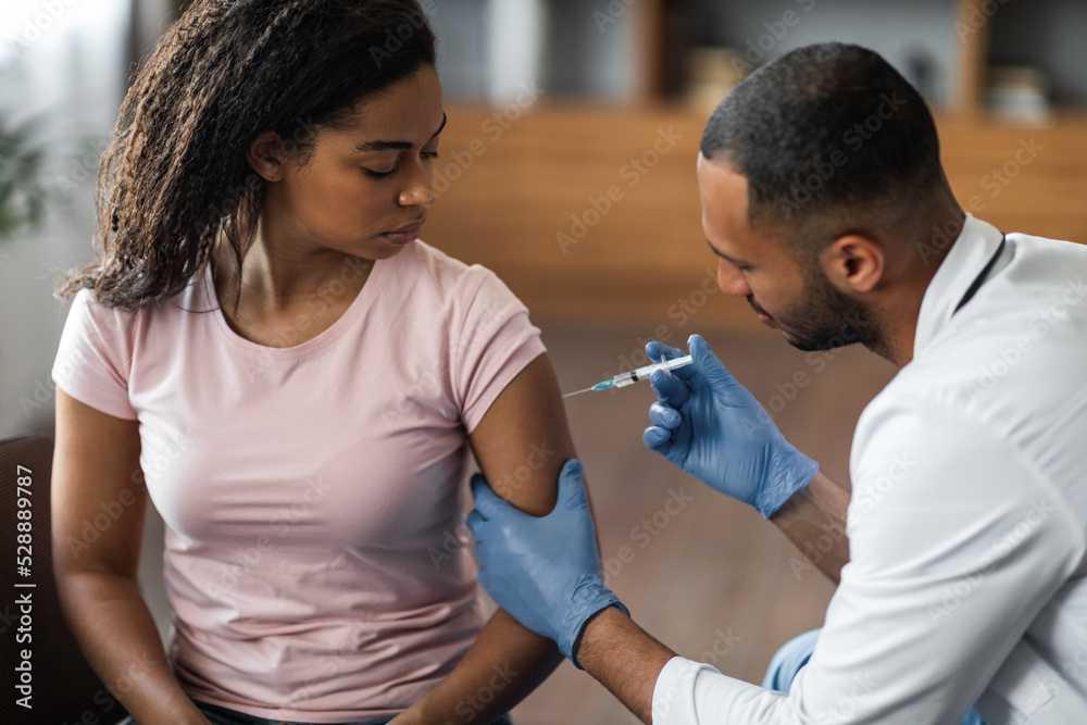Handsome black man making injection in shoulder for female patient ...