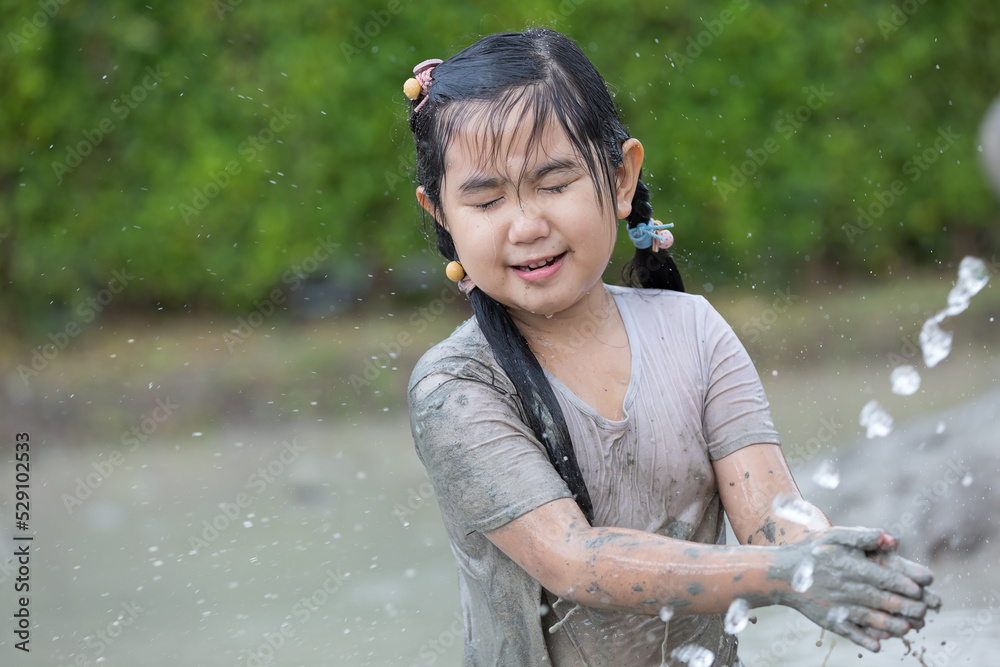 Happy little child girl playing in wet mud puddle during rainy season ...
